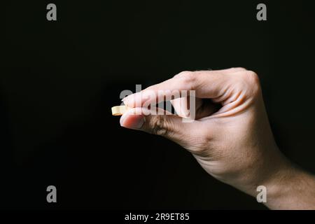A yellow pill is held by pointing and thumb fingers. Isolated black ...