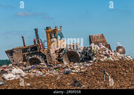 A soil compactor moving around and manipulating trash in the dirt on a ...