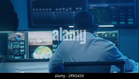African American flight control employee sits in front of computers ...