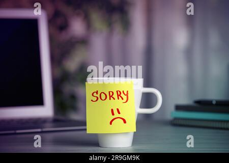 Apology. Sticky note with word Sorry and drawn sad face pinned on white ...