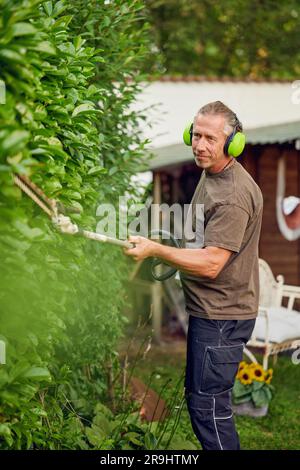 Gardener trimming a hedgerow using a hedge trimmer in the garden of a ...