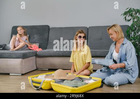 Mother with daughters packing yellow suitcase for travel. Family having ...