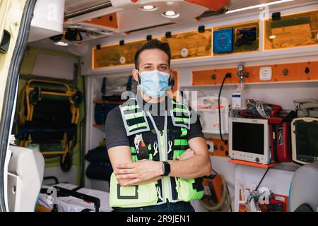 Paramedic in uniform crossing arms near blurred ambulance car outdoors ...