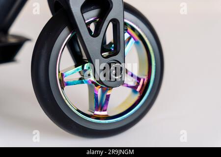 The front wheel of a rainbow-colored stunt scooter against a light ...