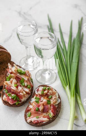 Shots with cold vodka and tasty sandwiches on white marble background ...