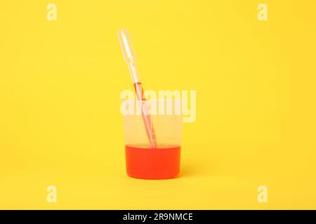 Beaker with liquid and stirring rod on yellow background, space for ...