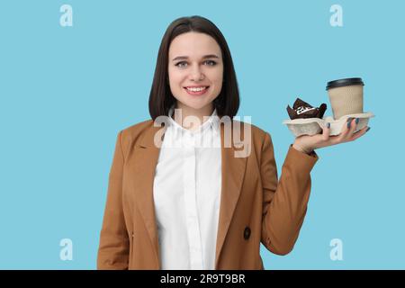 Happy young intern holding takeaway cup with hot drink and muffin ...