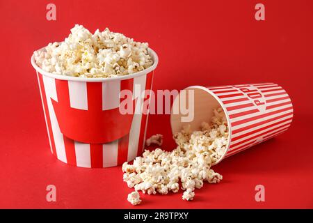 Buckets with delicious popcorn on red background. Spilled popcorn Stock ...