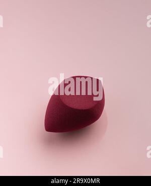 Cosmetic sponge in the shape of an egg on a pink background. Top view ...