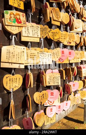 Rows of Japanese Shinto ema hanging on wooden board. Pink heart shaped ...