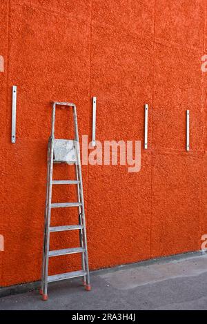 An aluminium ladder leaning against a red brick wall leading up to an ...