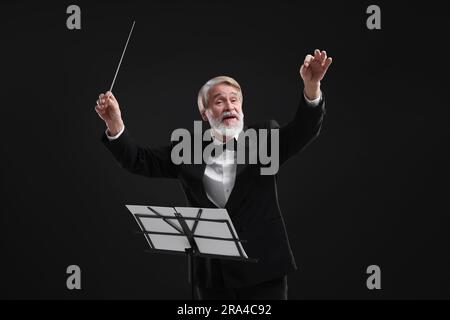Professional conductor with baton and note stand on black background ...