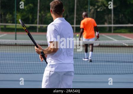 Diverse male tennis players walking with tennis rackets on outdoor ...