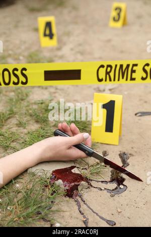 Evidence markers, yellow tape and knife on black slate table. Crime ...