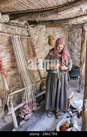 A reenactor portrays a first century woman grinding grain using a ...