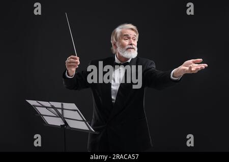 Professional conductor with baton and note stand on black background ...