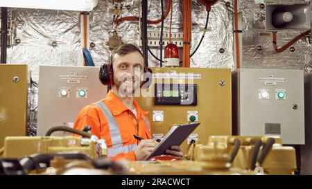 Young marine engineer making notes in engine room log book. Offshore ...