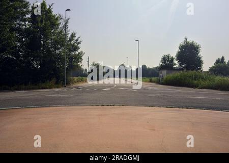 Road with an empty roundabout bordered by plants on a sunny day in the ...