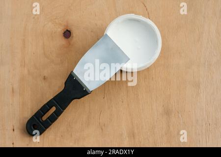 Construction putty knife and can of white putty on plywood surface ...
