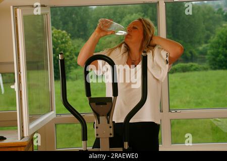 Woman on cross trainer, drinking water Stock Photo - Alamy