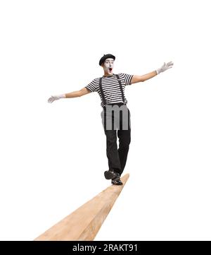 Cheerful mime walking on a wooden beam and carrying balloons and a gift ...