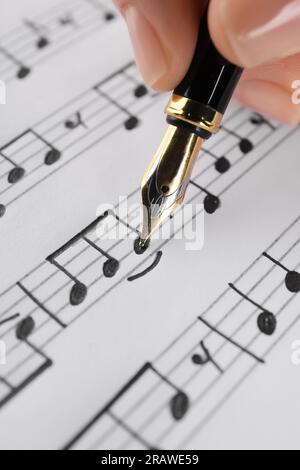 Woman writing musical notes with fountain pen on sheet of paper ...