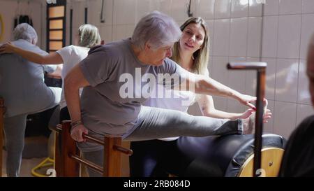 Female Pilates Coach guiding a senior woman to stretch body in ...