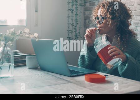 Young woman eating cookies and surfing internet on laptop at home Stock ...