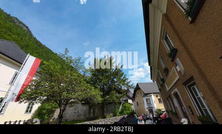Street life in Hallstatt; building, mountain, blue sky clouds, trees ...