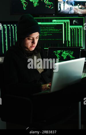 Informatic hacker woman typing code on laptop, at background a lot of ...