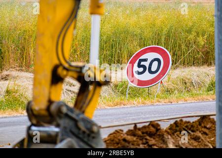 Arm of a mini digger and bucket with a speed limit sign at 50, road ...
