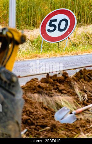 Arm of a mini digger and bucket with a speed limit sign at 50, road ...