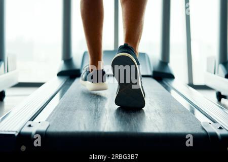 Close up male muscular feet in sneakers running on the treadmill at gym ...