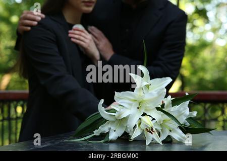 People near white lilies on tombstone at cemetery, closeup. Funeral ...