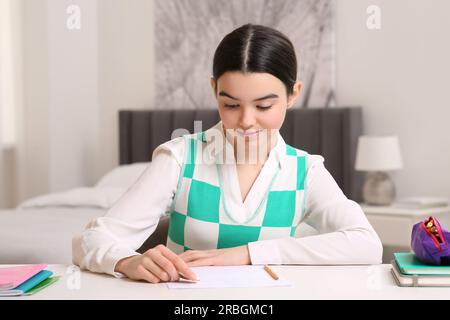 Teenage girl erasing mistake in her notebook at white desk indoors ...