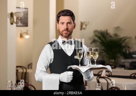 Butler holding tray with glasses of sparkling wine in restaurant. Space ...