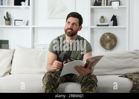 Soldier with magazine on sofa in living room, focus on pair of combat ...