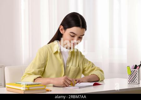 Teenage girl erasing mistake in her notebook at white desk indoors ...