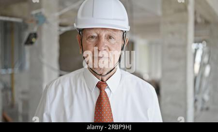 Senior grey-haired architect man holding blueprints using smartphone at ...
