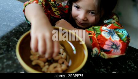 Little girl eating cashew nuts from bowl child eats healthy snack food ...