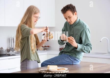 Young woman and man spreading nut butter onto toasts in kitchen. Banner ...