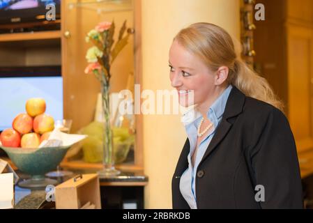 Beautiful stylish blond hotel receptionist standing behind the service ...