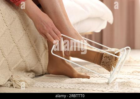 Woman putting on compression tights with stocking donner in bedroom ...
