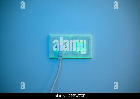 Green illuminated socket with plug inserted to symbolise power ...