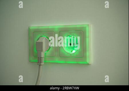 Green illuminated socket with plug inserted to symbolise power ...