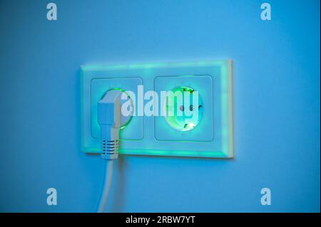 Green illuminated socket with plug inserted to symbolise power ...