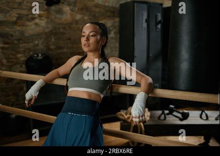 Athletic female fighter with bandaged hands standing leaned at wooden ...