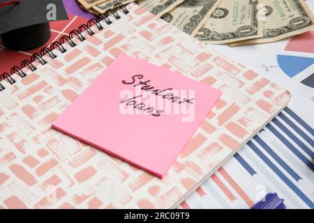 Sticky note with text STUDENT LOANS, notebook and dollar banknotes on ...