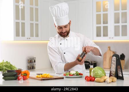 Professional chef adding pepper into delicious salad at marble table in ...