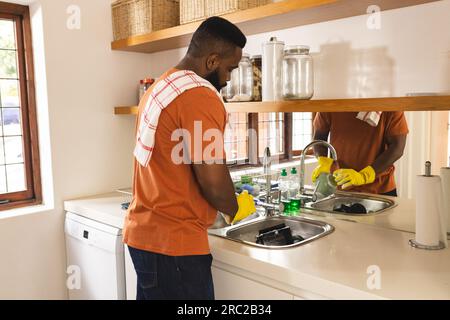 Focused african american man with towel on arm washing dishes in ...